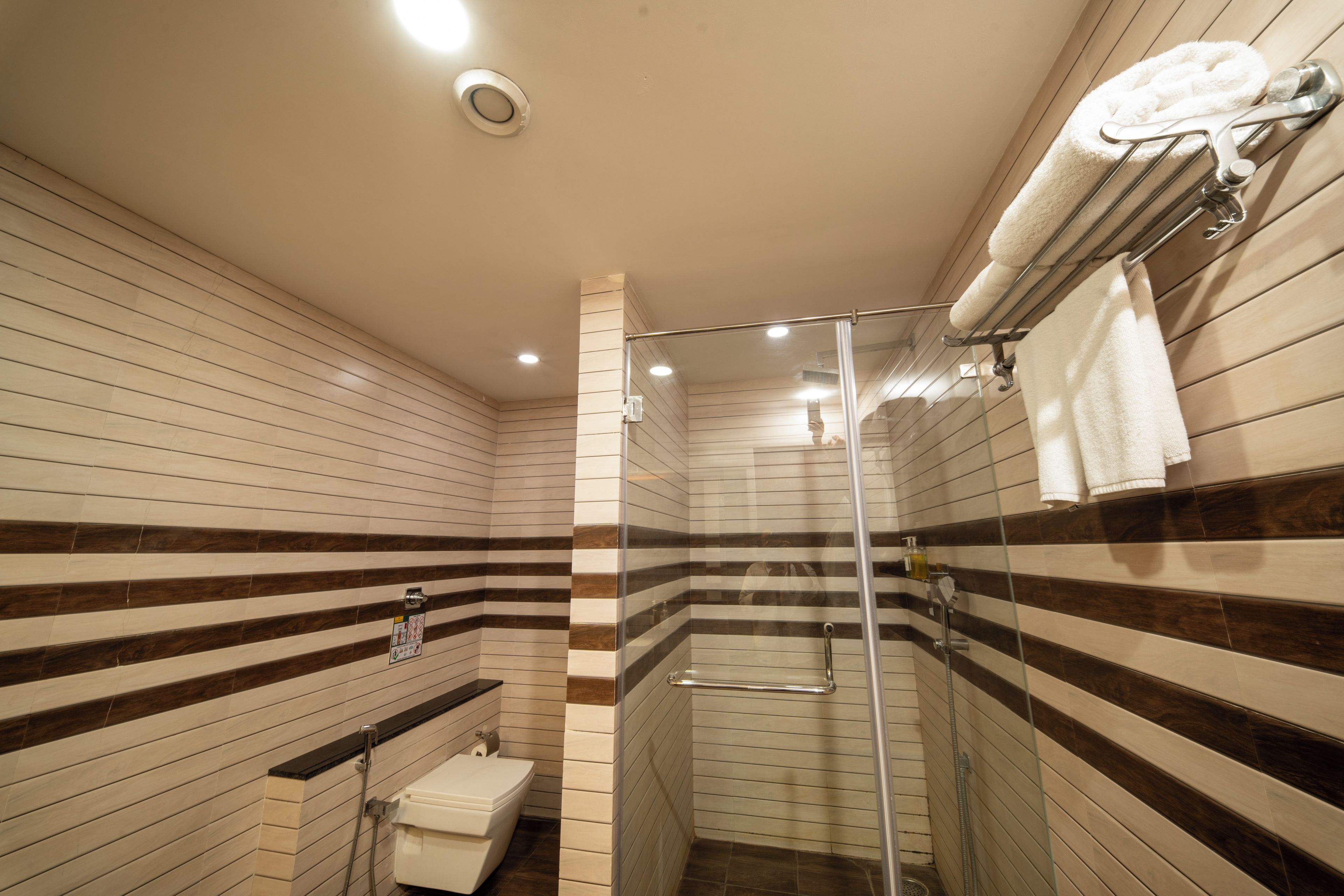 Um banheiro moderno com paredes de azulejos listrados, box de vidro, vaso sanitário e porta-toalhas.