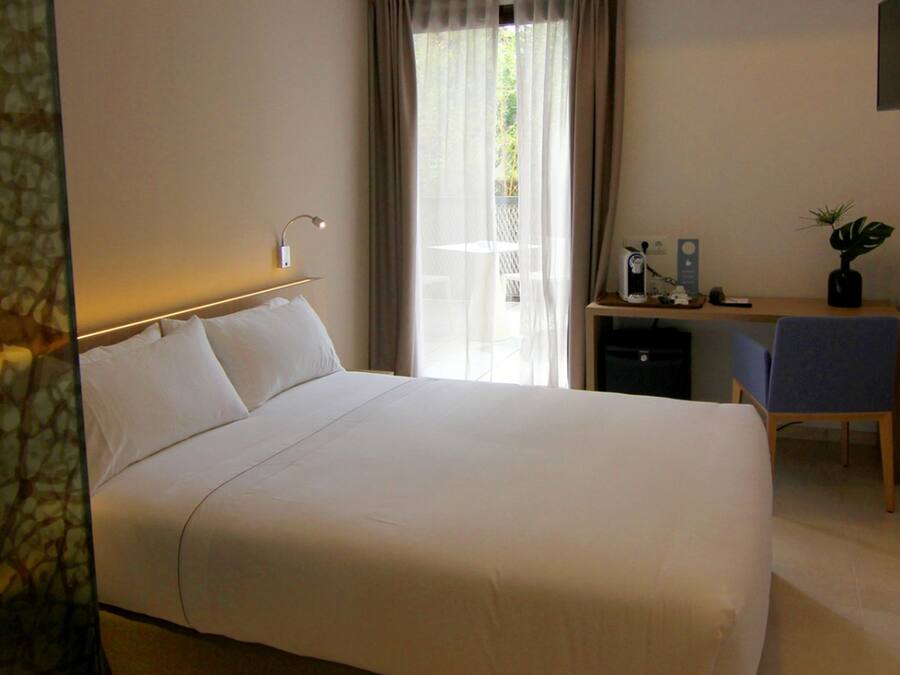 Quarto de hotel com uma cama grande, uma escrivaninha com cadeira, televisão na parede e uma janela com cortinas.