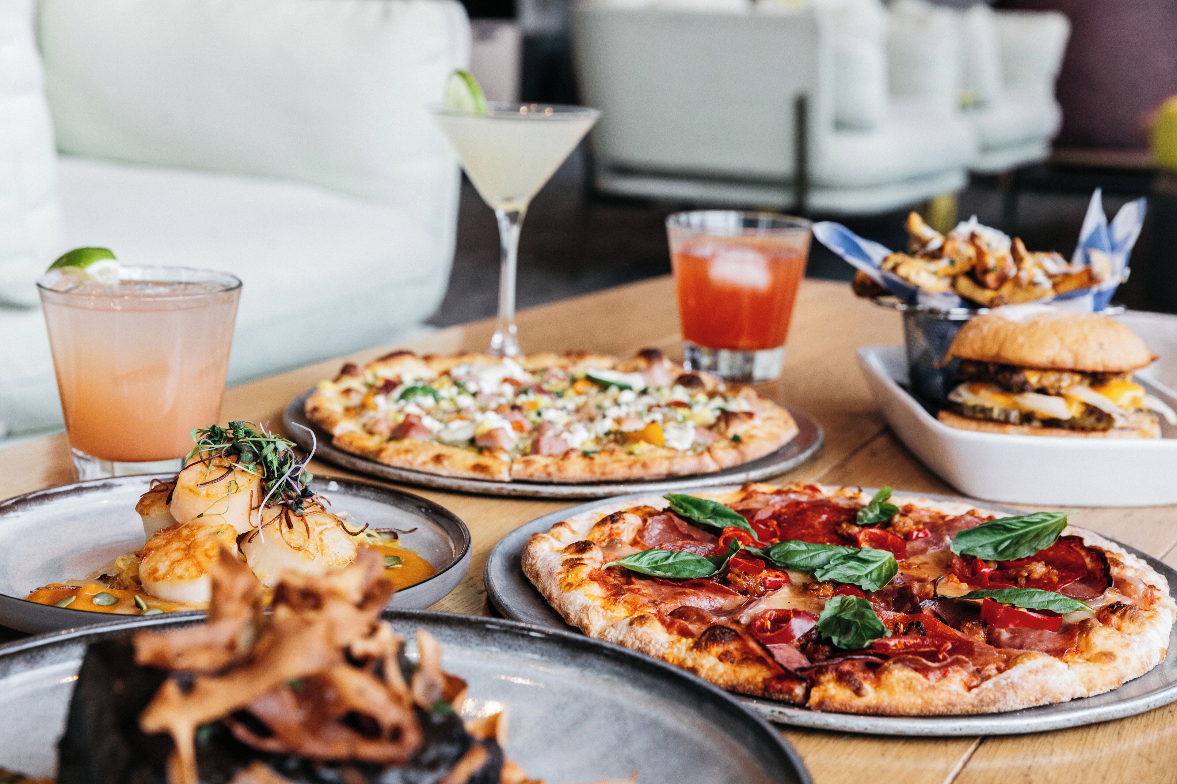 Uma mesa de jantar com várias pizzas, um copo de martini e um copo de chá gelado.
