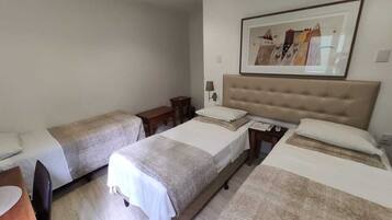 Quarto de hotel com três camas de solteiro, uma secretária pequena e uma cadeira.