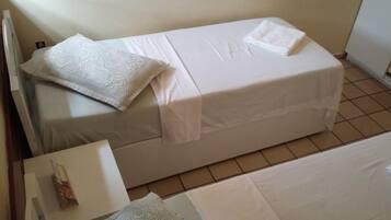Uma cama pequena e bem arrumada, com almofada e toalha brancas dobradas.