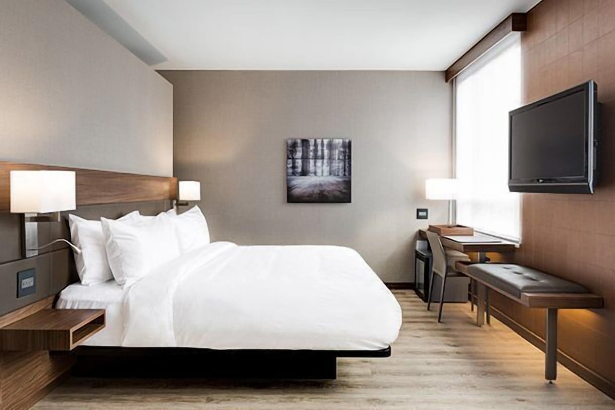 Quarto de hotel moderno com uma cama grande, mesas de cabeceira, uma escrivaninha e uma TV.