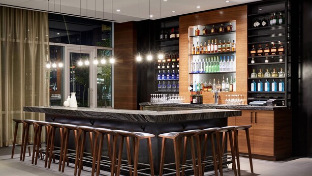 Uma área de bar moderna com bancada de mármore, banquetas de madeira e uma prateleira de bebidas bem abastecida.