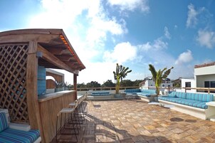 Um terraço no telhado com piso de madeira, assentos em azul listrado e uma pérgola de madeira.