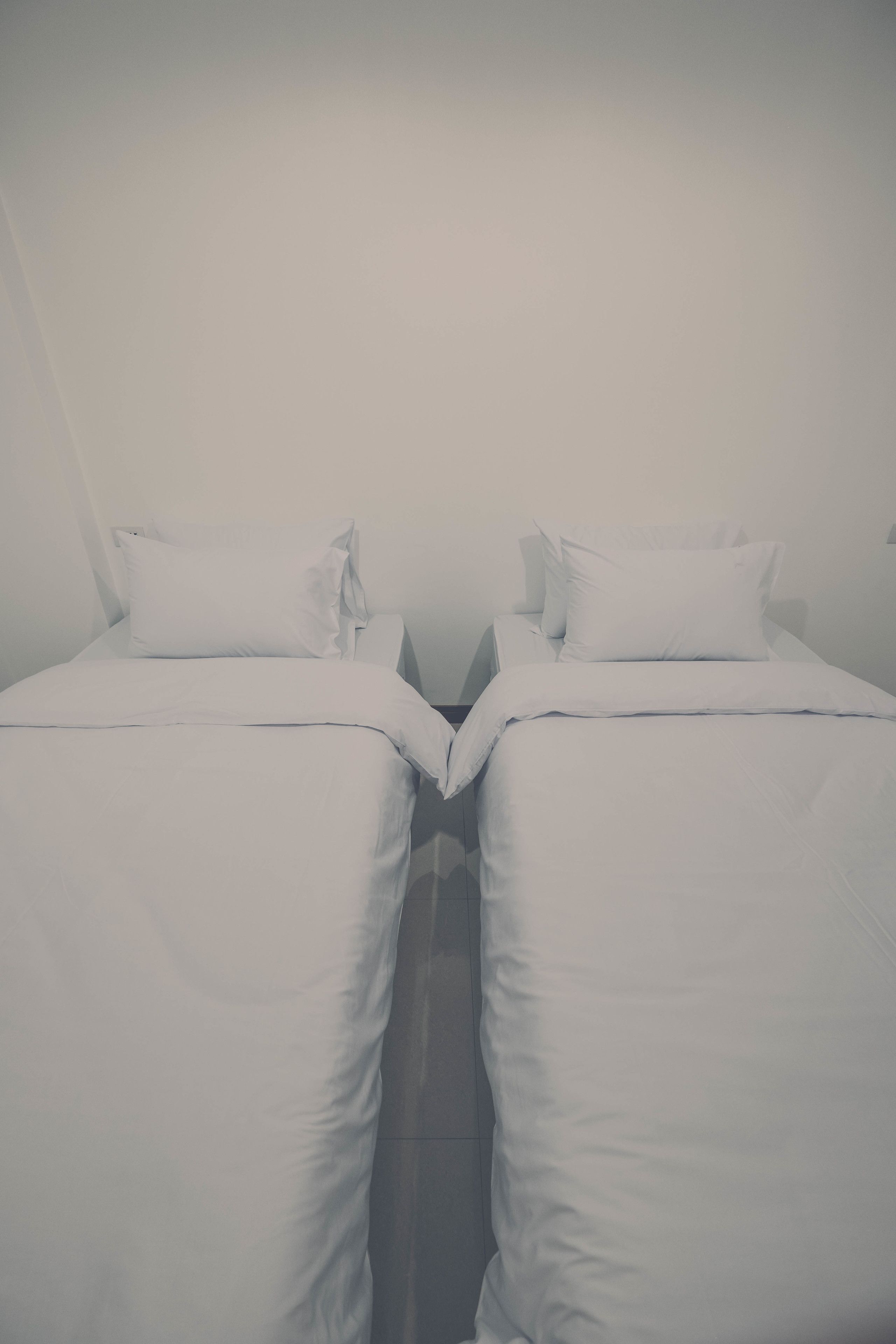 Quarto com duas camas, cada uma com roupa de cama e almofadas brancas.