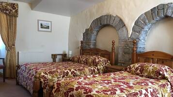 Quarto com duas camas de madeira, um arco de pedra, um candelabro e um radiador.
