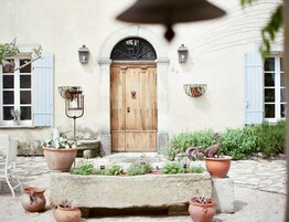 Um pátio rústico com porta de madeira, plantas em vasos e um banco de pedra.