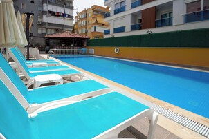Piscina com espreguiçadeiras e guarda-sóis, rodeada por edifícios altos.