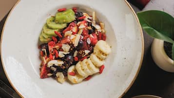 Um prato branco com kiwi fatiado, morangos e banana, coberto com sementes e nozes.