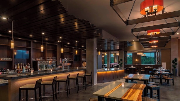 Uma área de bar moderna com um balcão comprido, vários bancos altos e uma tela de televisão.