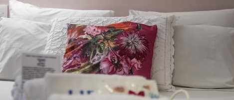 Uma cama de hotel com roupa de cama branca, um travesseiro floral e uma placa com a inscrição 'Hotel da Praia'.