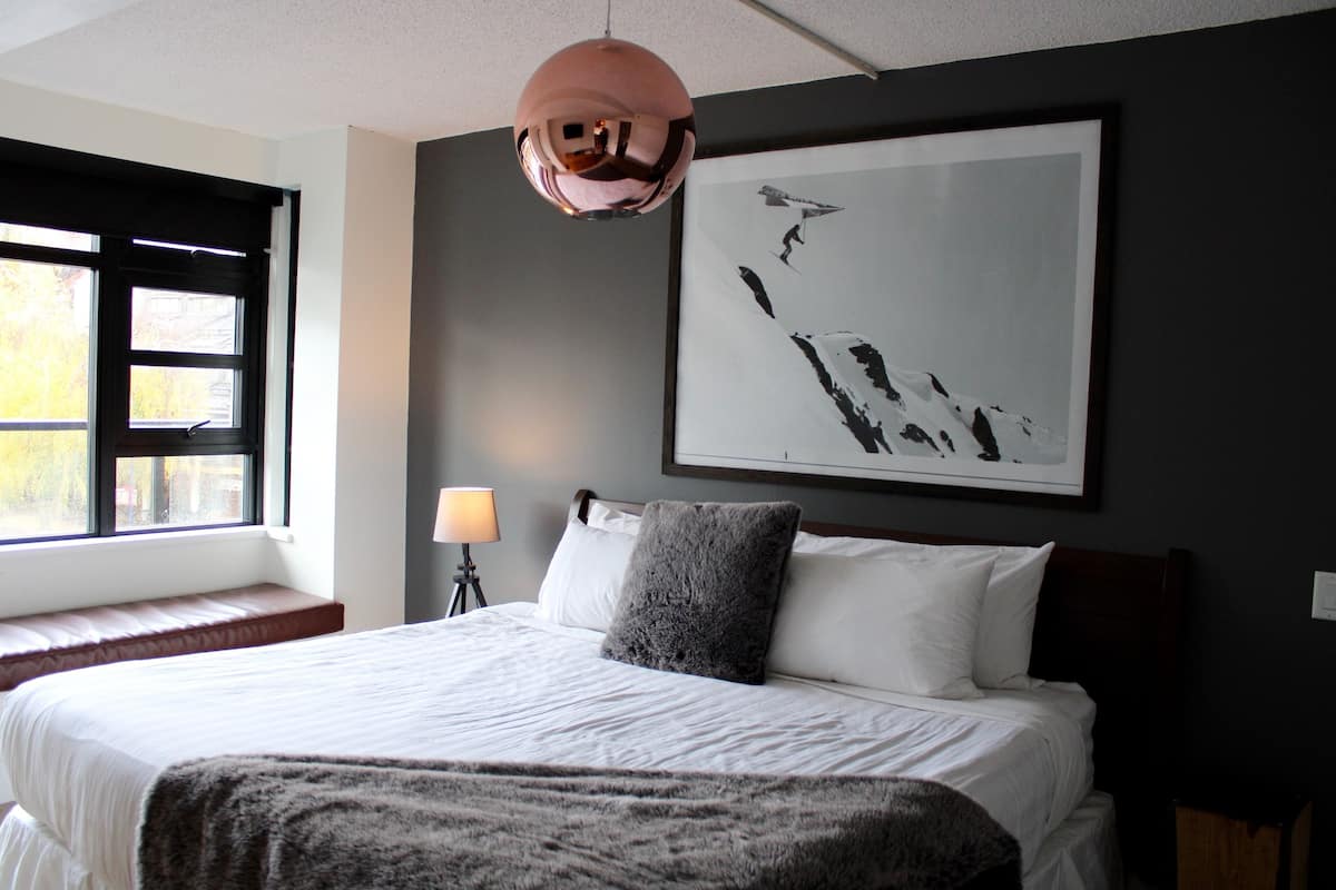 Quarto com uma cama grande, mesa de cabeceira, abajur e janela com persianas.