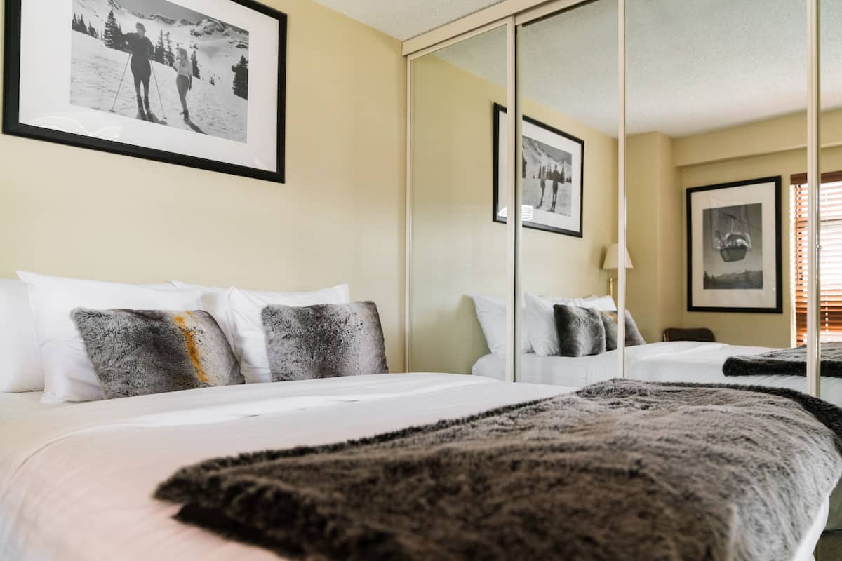 Quarto de hotel com cama, um espelho grande e duas fotografias emolduradas na parede.