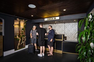 Uma área de recepção com um letreiro 'CHECK IN', uma decoração de parede em madeira e um balcão de atendimento.