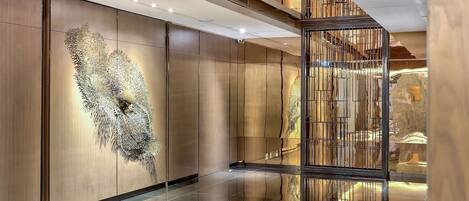 Um lobby moderno com piso refletivo, uma grande obra de arte abstrata na parede e vista para uma escadaria.