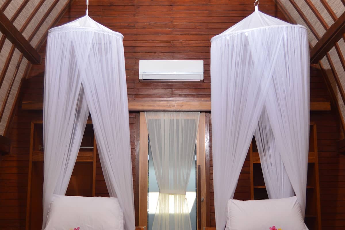 Quarto com duas camas, cada uma com dossel, paredes de madeira e um pequeno aparelho de ar condicionado na parede.