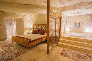 Quarto com cama de madeira, um separador decorativo, banheiro com banheira e um tapete estampado.