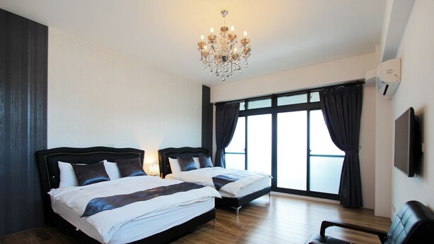 Quarto de hotel com duas camas, um candelabro, uma janela grande com cortinas, uma TV de tela plana e um espaço de estar.