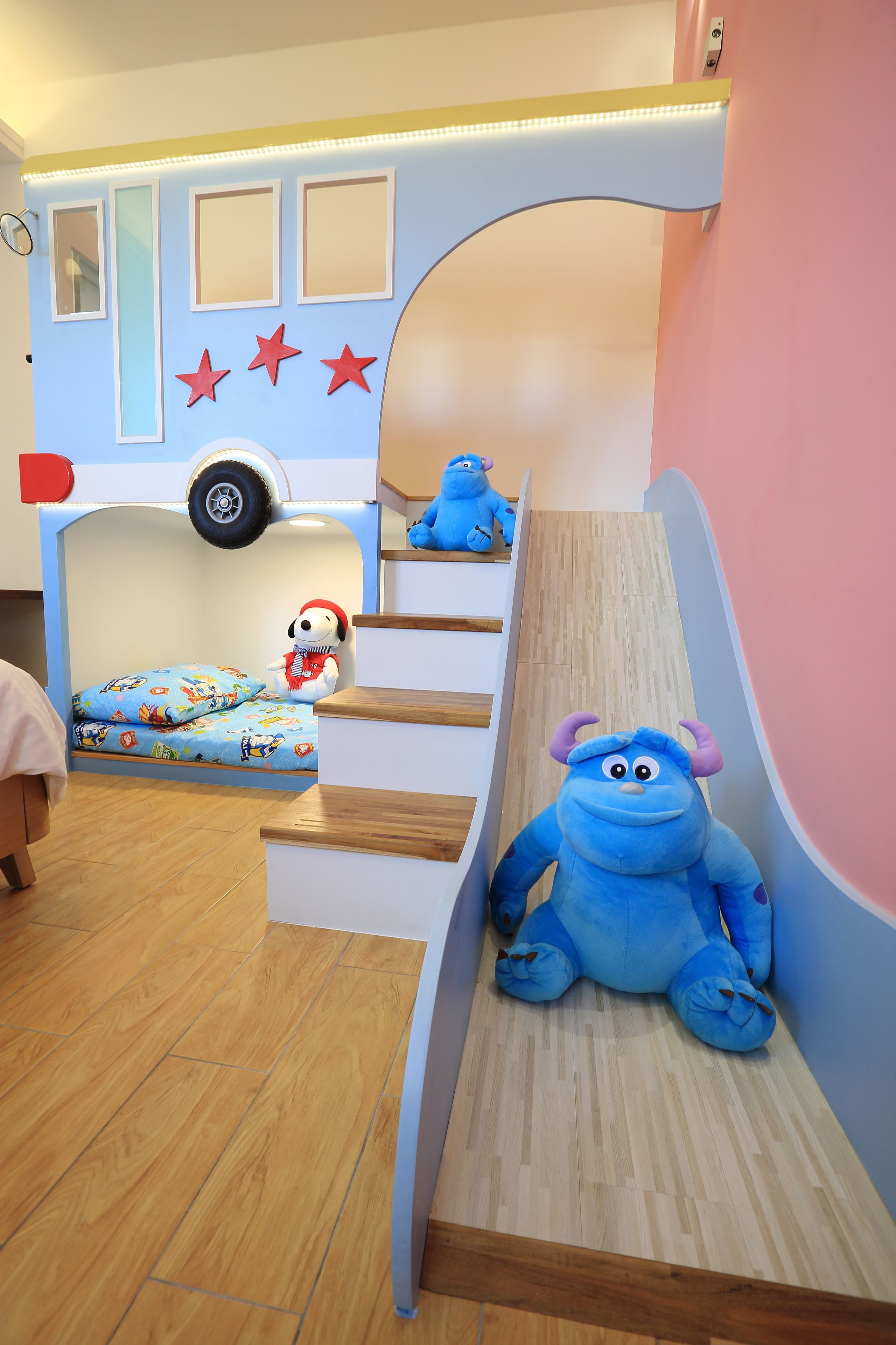 Espaço infantil com escorrega, cama com colchão temático de desenho animado e um brinquedo de pelúcia grande.