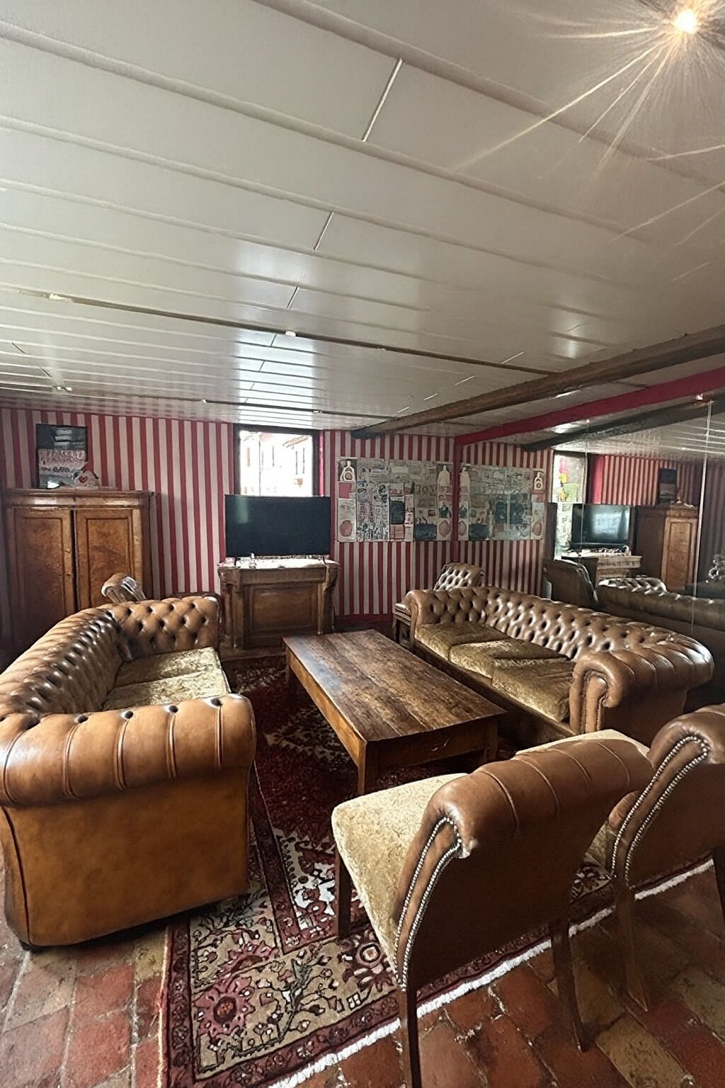 Sala de estar com papel de parede listrado, mesa de centro de madeira, sofás de couro e uma televisão.