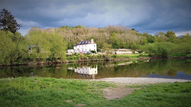 Uma casa branca com um amplo jardim e um lago em primeiro plano.