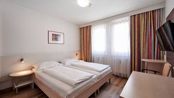 Quarto de hotel com duas camas, uma escrivaninha, televisão e um quadro na parede.