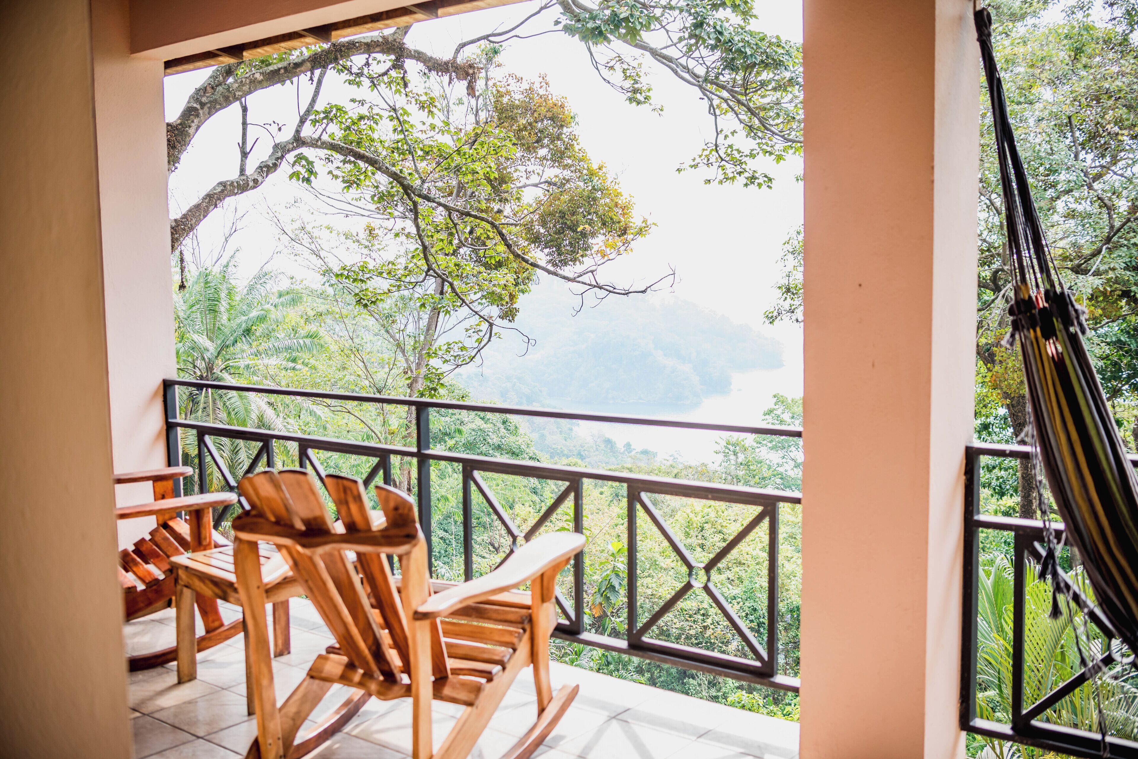 Varanda com cadeiras de madeira e uma rede, com vista para uma paisagem verde exuberante.