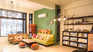 Uma sala de estar bem iluminada com uma parede verde de destaque, um sofá com almofadas em formato de rosquinha, uma mesa de centro e uma estante cheia de livros e brinquedos.