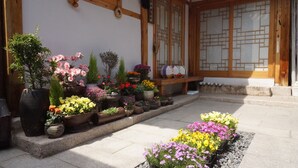 Um edifício japonês tradicional com um pátio ladrilhado, vigas de madeira e diversos vasos com plantas e flores.
