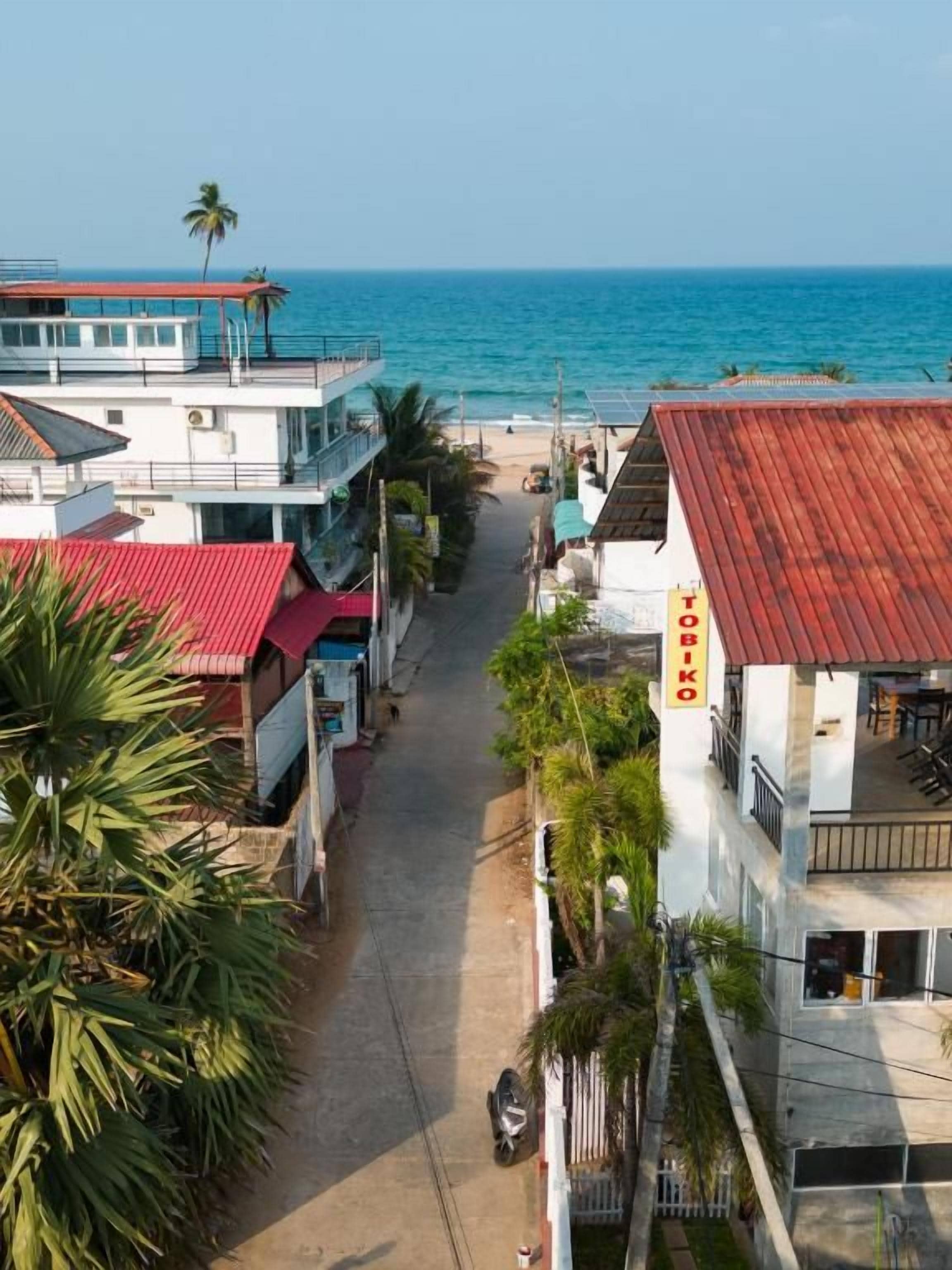 Uma rua costeira com edifícios, céu claro e o oceano ao fundo.