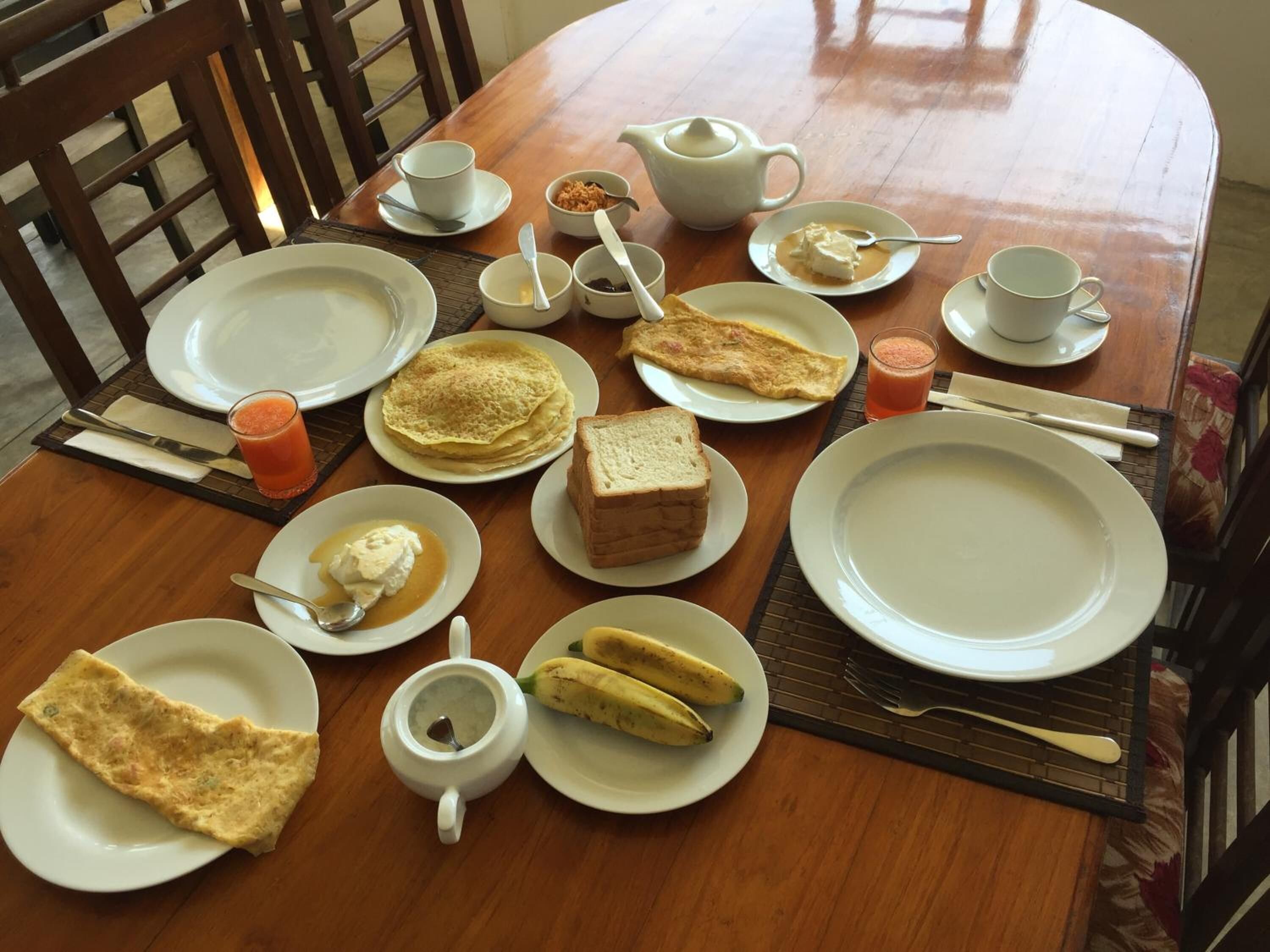 Mesa de jantar posta com pratos, tigelas, xícaras e um bule, sugerindo um ambiente de café da manhã.