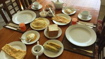 Mesa de jantar posta com pratos, tigelas, xícaras e um bule, sugerindo um ambiente de café da manhã.