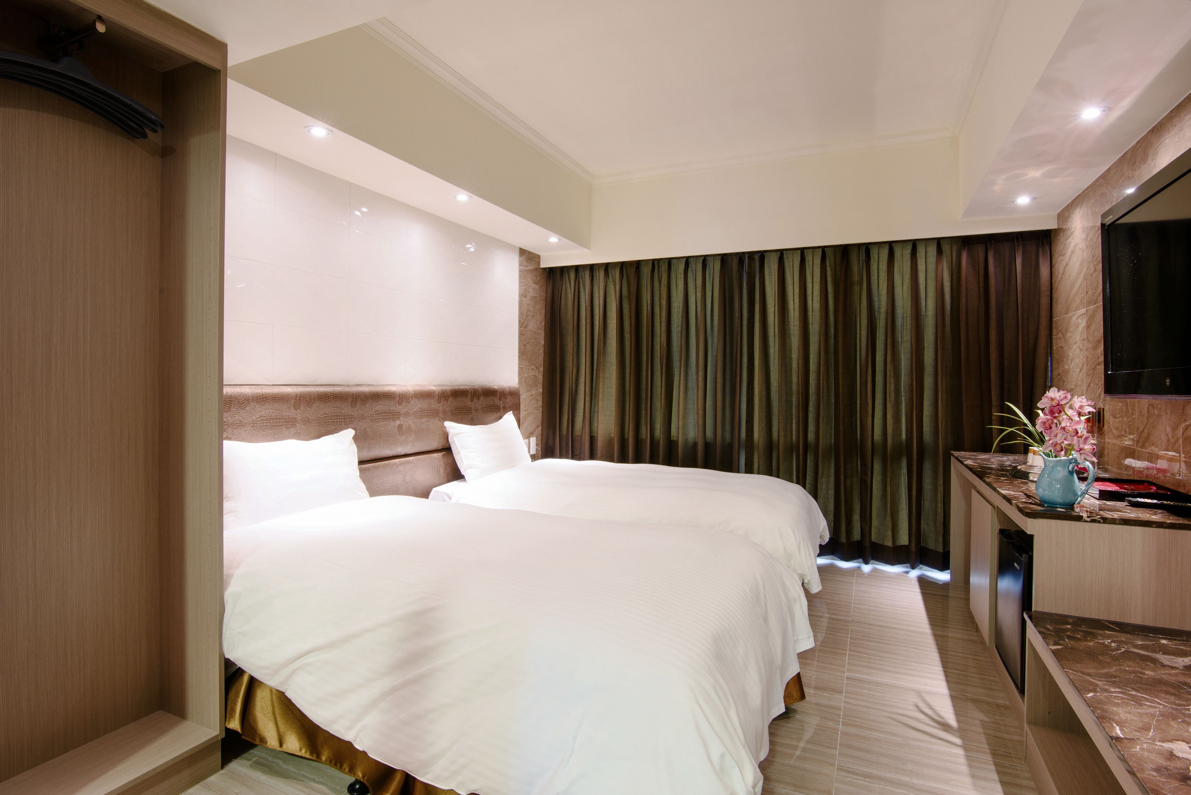 Quarto de hotel com duas camas, um minibar e uma janela grande com cortinas.
