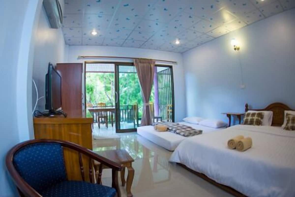 Quarto de hotel com cama, escrivaninha, cadeira e varanda com vista para vegetação.
