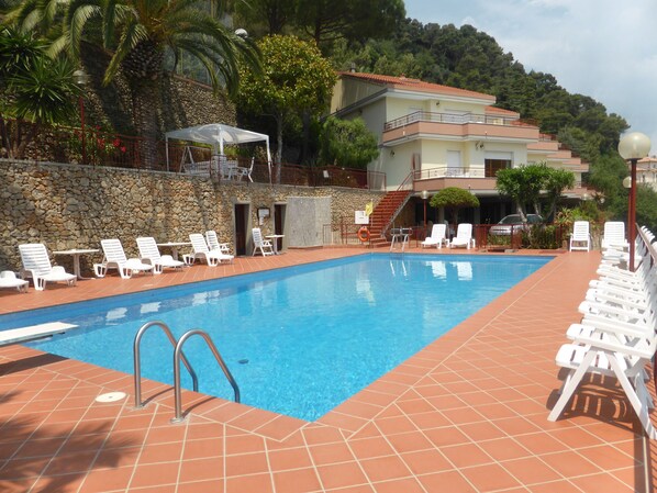 Piscina com espreguiçadeiras brancas e um muro de pedra.