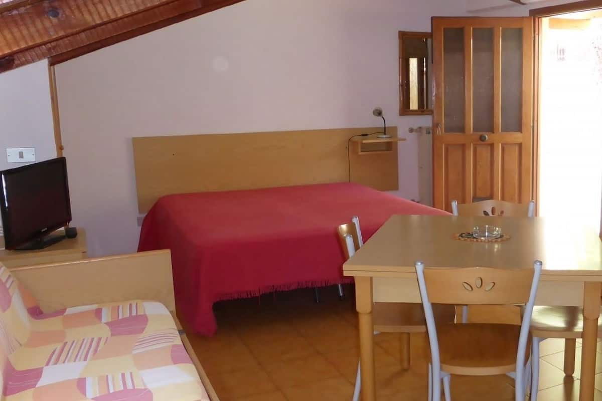 Um quarto com uma cama, uma mesa com cadeiras, uma televisão e um guarda-roupa.
