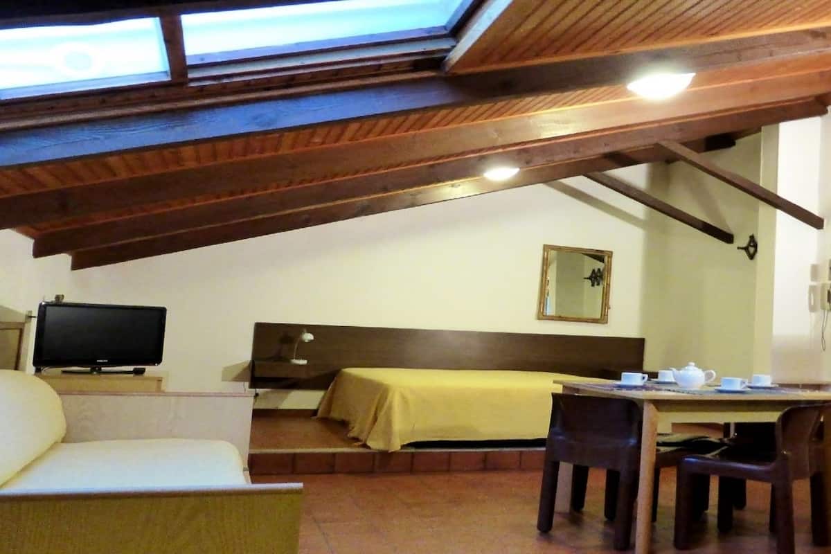 Um quarto com uma cama, uma escrivaninha com cadeiras, uma televisão e uma janela com vigas de madeira.