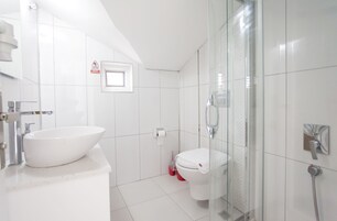 Um banheiro moderno com uma pia grande e branca, vaso sanitário e área de chuveiro com divisória de vidro.
