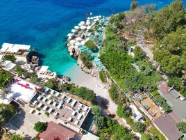 Vista aérea de um resort à beira-mar, com praia, áreas de descanso e piscina.