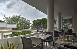 Varanda com mesa posta para dois, cadeiras e vista para árvores e edifícios.