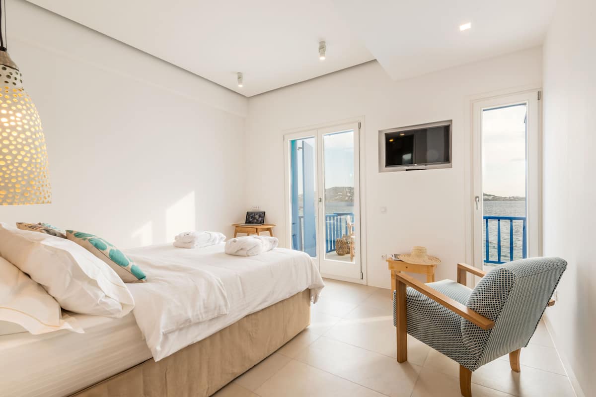 Quarto com cama, poltrona, televisão e varanda com vista.