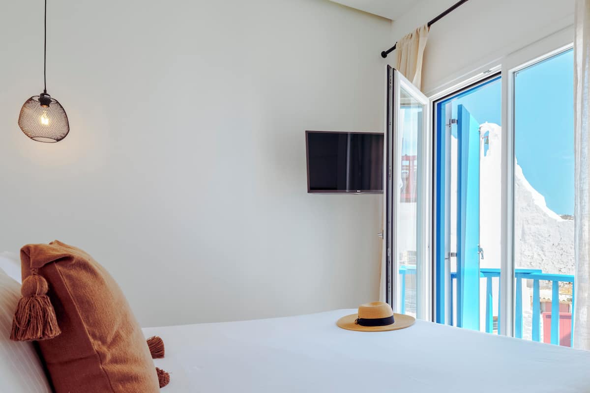 Quarto com cama, TV, janela com vista para um edifício branco e luminária pendente.