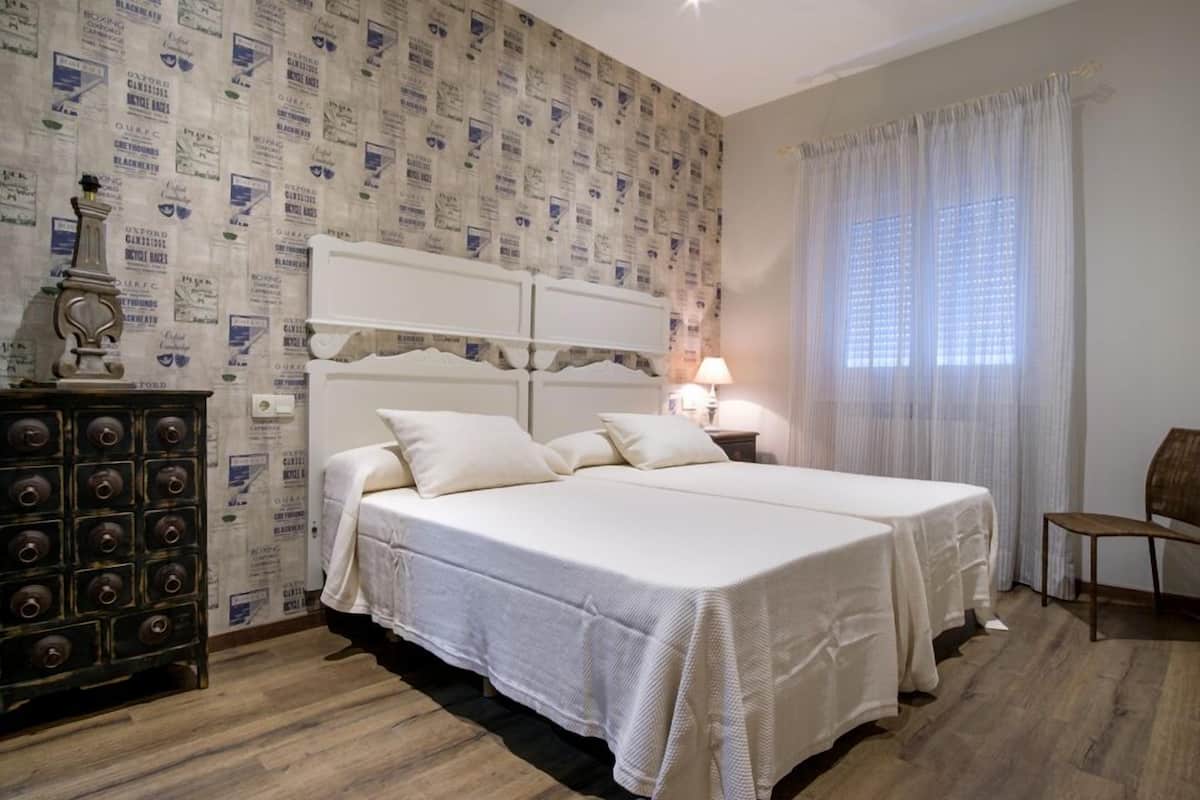 Quarto com cama grande, mesa de cabeceira, cômoda e janela com cortinas.
