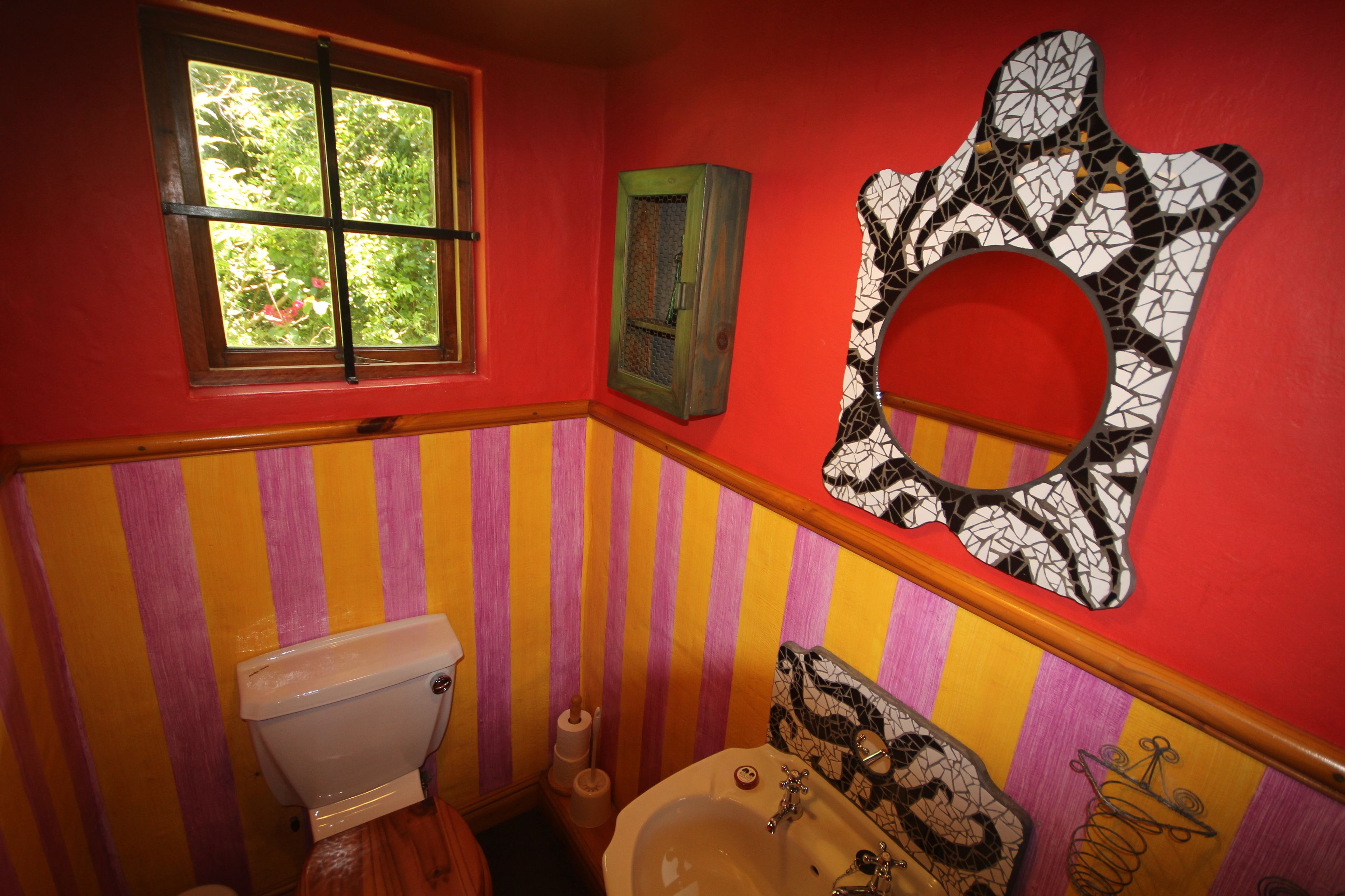 Casa de banho com design de parede riscada, sanita, lavatório e janela com vista para vegetação.