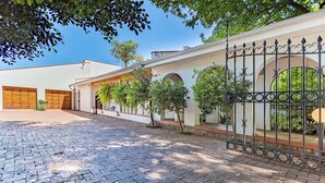 Um pátio pavimentado com portão e entrada, um edifício com janelas em arco e um caminho de tijolos.