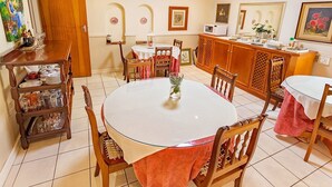 Uma sala de jantar com uma mesa redonda, cadeiras, um armário de madeira e um micro-ondas na parede.