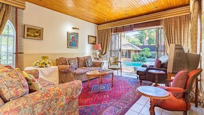 Uma sala de estar ampla com teto de madeira, vista para a piscina e uma televisão.