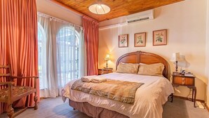 Quarto com cama de madeira, uma cadeira, mesa de cabeceira e janela com cortinas.