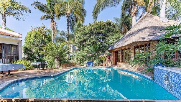 Piscina rodeada por vegetação exuberante e uma construção com telhado de palha.