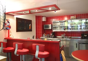 Uma área de bar com banquetas vermelhas, um cardápio em lousa e um micro-ondas.